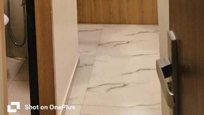 Corredor estreito que dá para um quarto, com uma cama, janela com persianas e área de chuveiro.