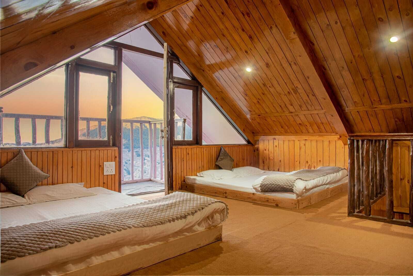 Quarto de sótão aconchegante com duas camas, paredes de madeira e amplas janelas com vista para a paisagem.