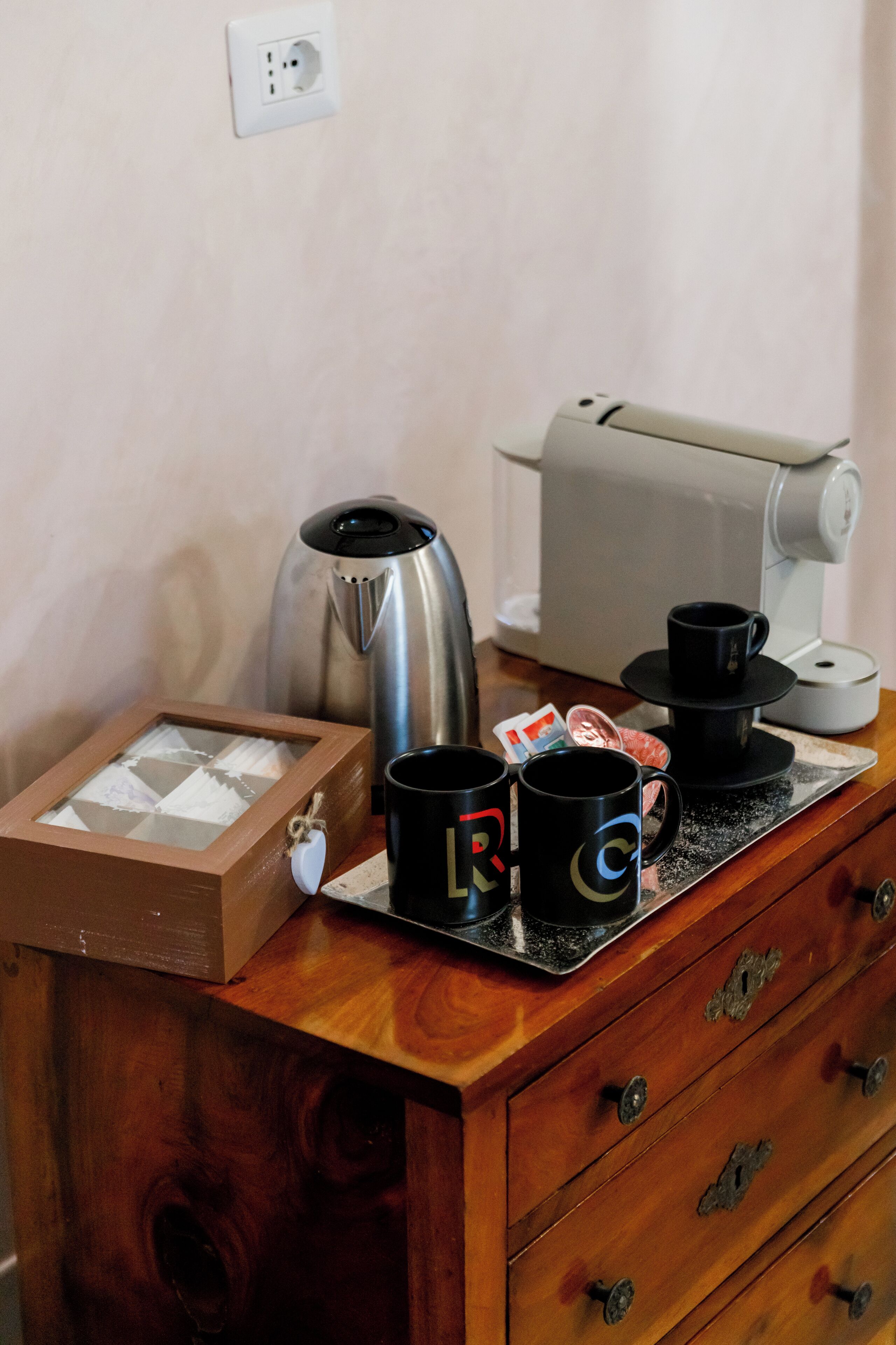 Uma cômoda de madeira com uma moldura, uma chaleira, duas canecas pretas e uma cafeteira.