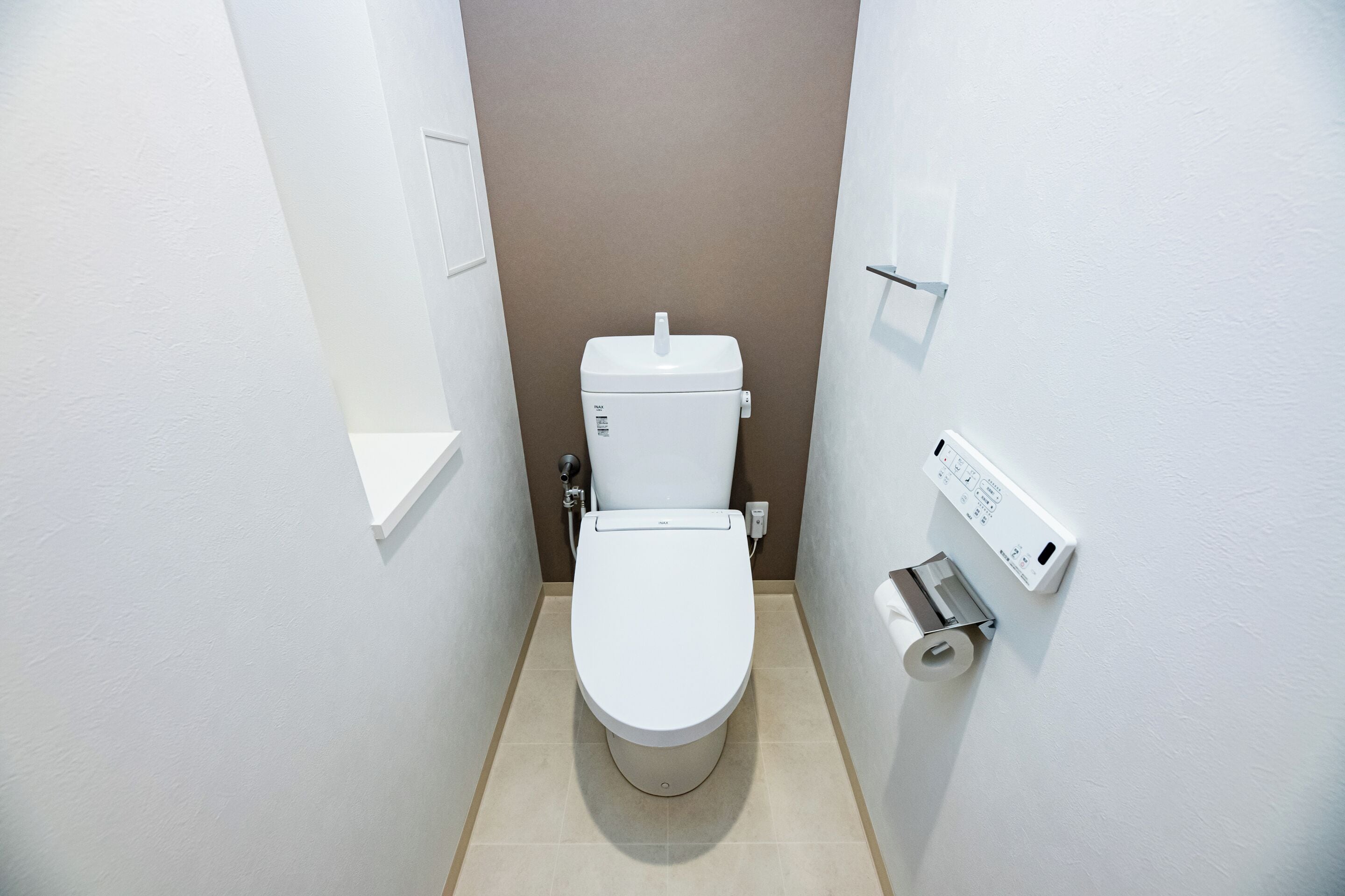 Casa de banho pequena e moderna com sanita branca, suporte de papel higiénico e um botão de descarga na parede.