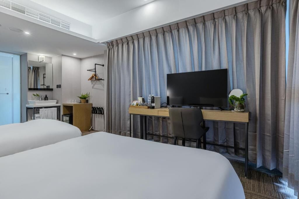 Quarto de hotel com cama, escrivaninha com televisão, pequeno espaço de cozinha e banheiro.