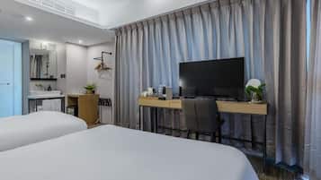 Quarto de hotel com cama, escrivaninha com televisão, pequeno espaço de cozinha e banheiro.
