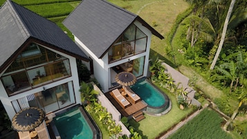 Uma casa de dois andares com piscina, área de estar externa e vegetação exuberante.