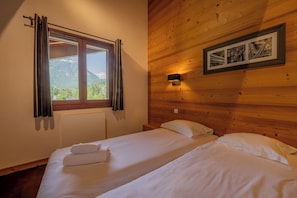 Quarto com duas camas, janela com cortinas, quadro pendurado na parede e painel de parede de madeira.