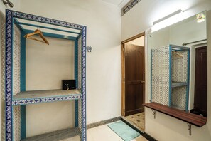 Uma casa de banho com chuveiro revestido a azulejos azuis e brancos, porta de madeira, espelho com moldura decorativa e uma pequena prateleira com uma toalha.