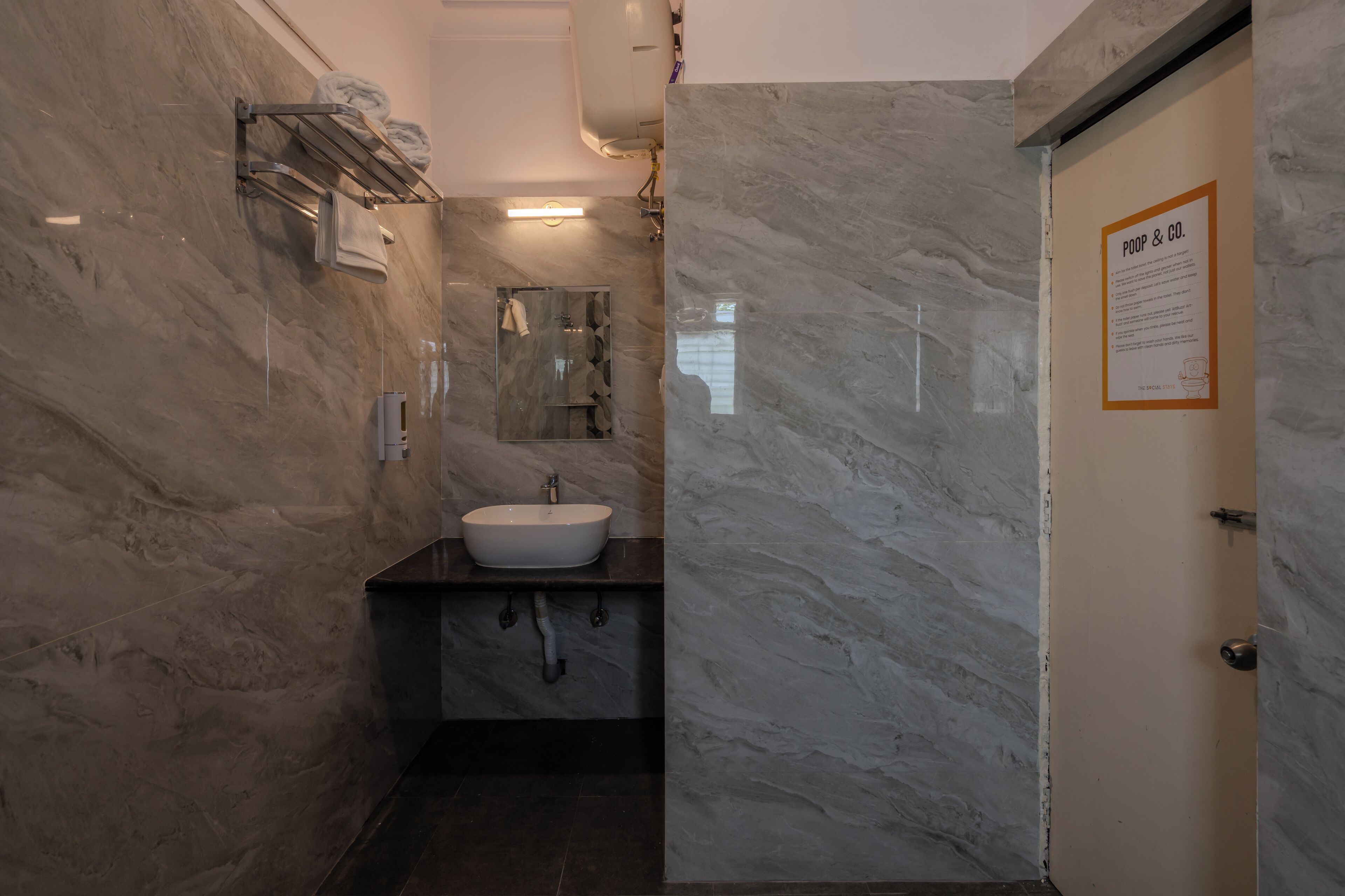 Uma casa de banho com parede de mármore, lavatório, suporte de toalhas e porta com um aviso.