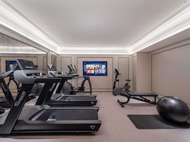 Sala de ginástica com esteiras, elíptico, bicicleta ergométrica e TV exibindo vídeos de exercícios.