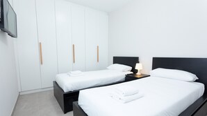 Quarto de hotel moderno com duas camas, uma televisão e um guarda-roupa com portas deslizantes.