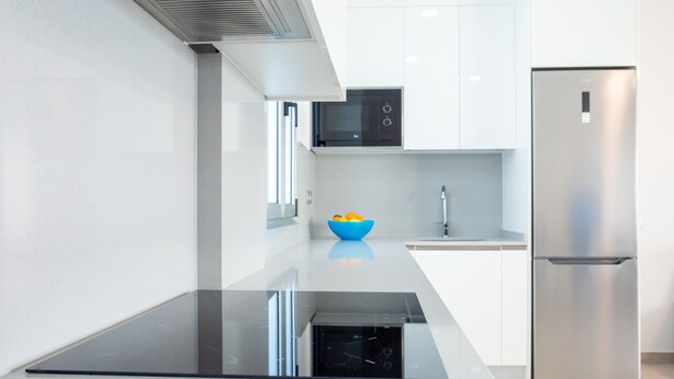 Uma cozinha moderna com um fogão por indução preto, uma geladeira de aço inoxidável e armários brancos.