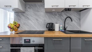 Cozinha moderna com bancada de madeira, eletrodomésticos de aço inoxidável e painel de fundo de mármore.
