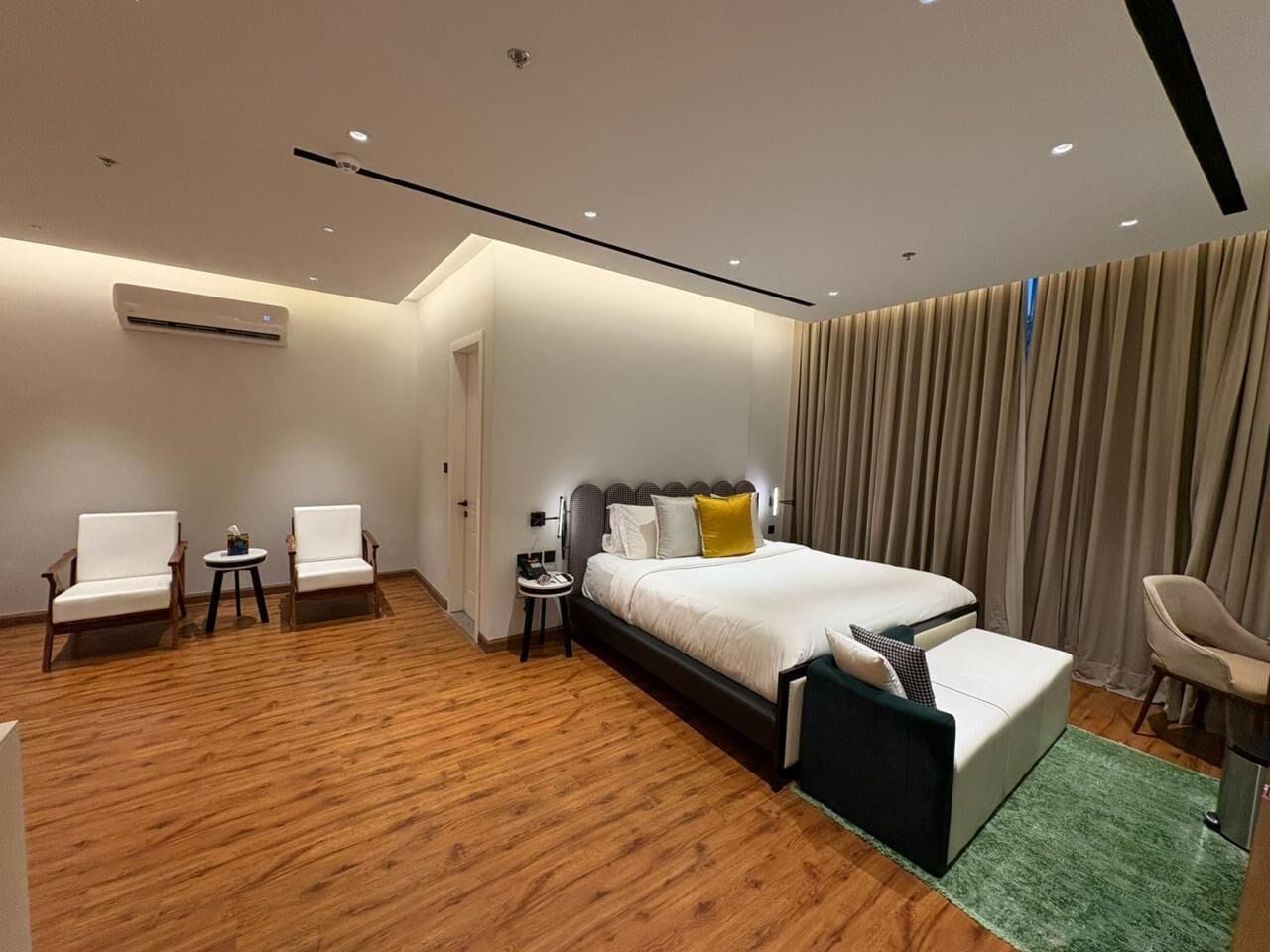 Quarto de hotel moderno com uma cama grande, duas poltronas, uma pequena mesa e uma escrivaninha.