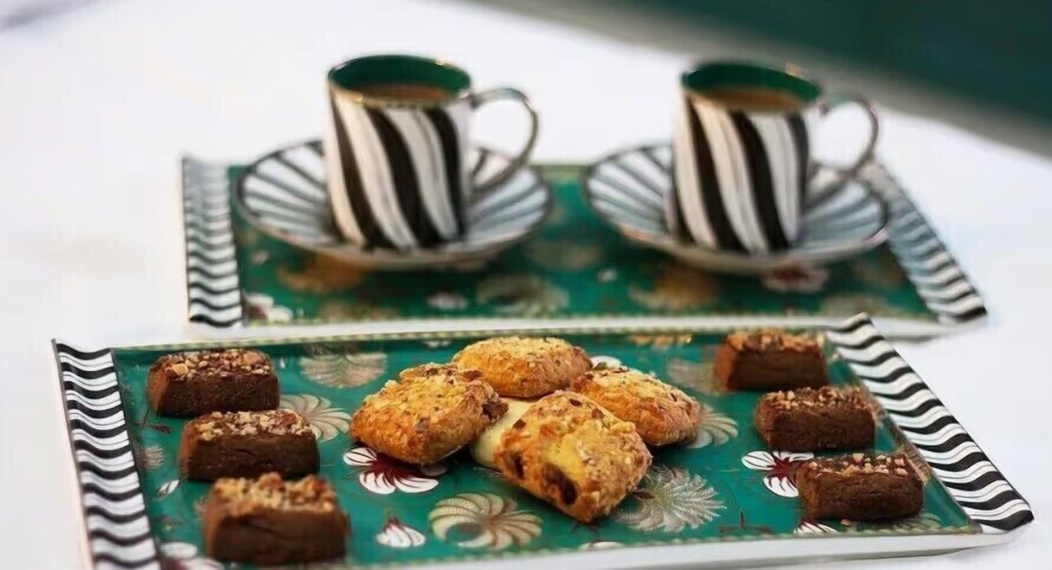 Uma bandeja com doces e duas xícaras de café sobre uma toalha de mesa estampada.