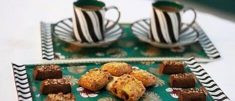 Uma bandeja com doces e duas xícaras de café sobre uma toalha de mesa estampada.