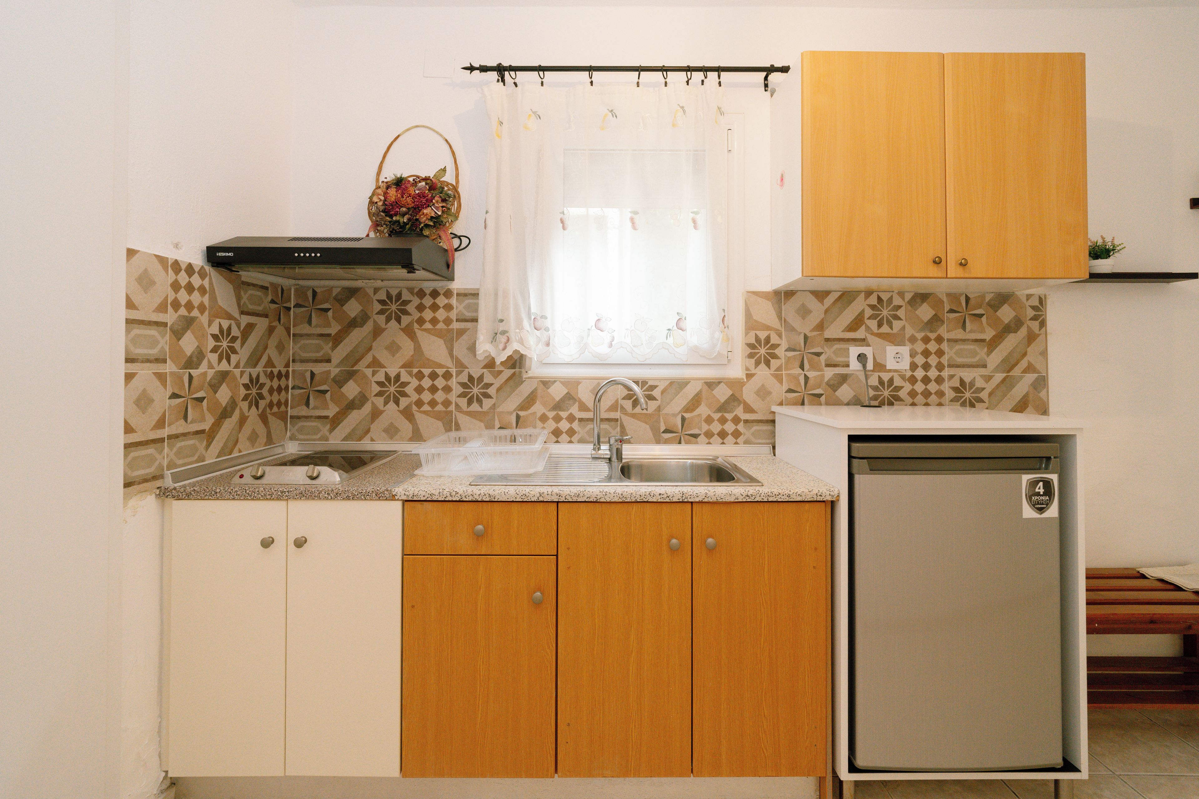 Cozinha compacta com máquina de lavar louça embutida, janela com cortina e azulejos de parede estampados.
