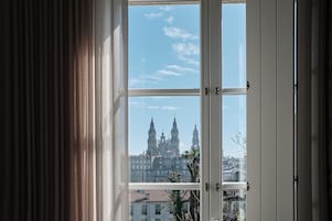 Janela com vista para uma catedral histórica com duas torres, cortinas e uma planta no interior.