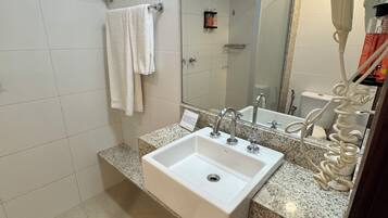 Casa de banho com lavatório branco, espelho e secador de cabelo.