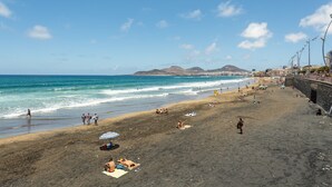 Uma praia com pessoas tomando sol e caminhando pela orla.