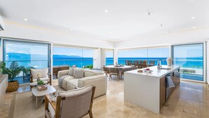 Ampla sala de estar com uma ilha grande, espaço para sentar e vista para o mar.