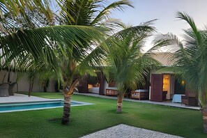 Uma área externa bem cuidada com piscina, palmeiras e um edifício com porta vermelha.
