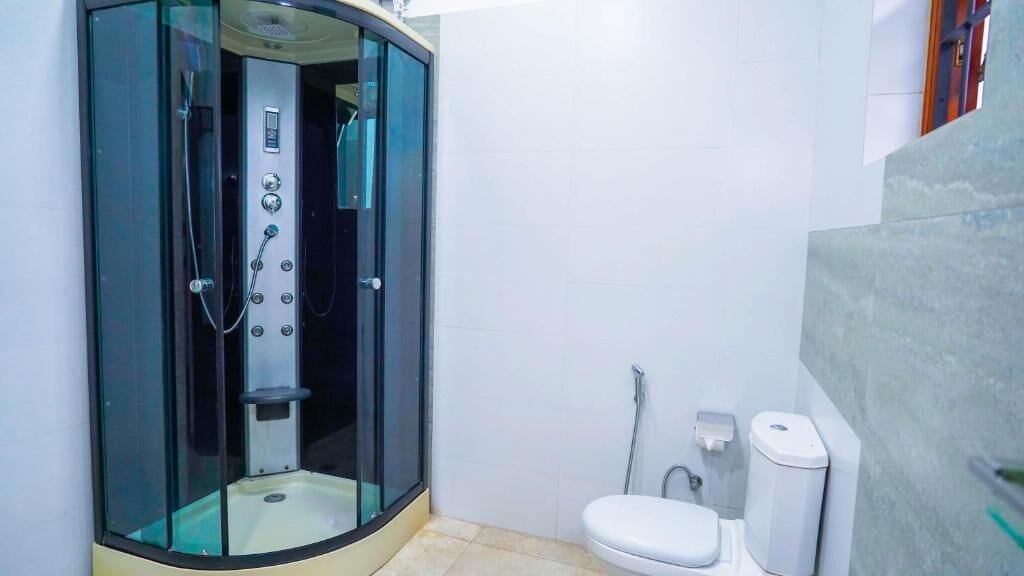Uma casa de banho moderna com cabine de chuveiro em vidro, sanita e secador de mãos.