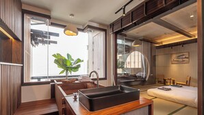 Uma casa de banho moderna com toucador de madeira, lavatório preto e uma janela ampla com uma planta.