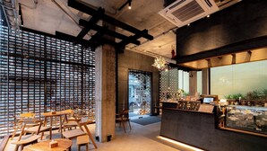 Um café moderno com mesas e cadeiras de madeira, um balcão com vitrine e uma parede decorativa com padrão de grade.