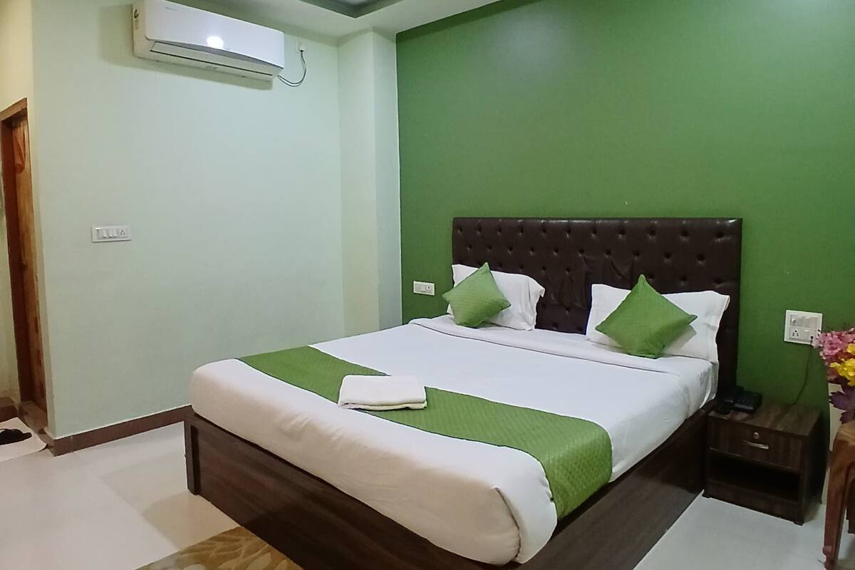 Quarto bem arrumado com cama, paredes verdes, ventilador de teto e ar condicionado.