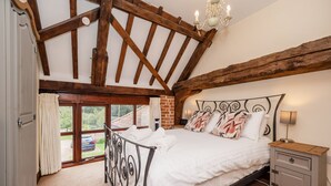 Quarto com cama, mesa de cabeceira, lustre e vista para o exterior.