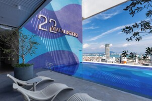 Uma área de piscina moderna ao ar livre com vista para o horizonte da cidade, uma grande planta em vaso e espreguiçadeiras.