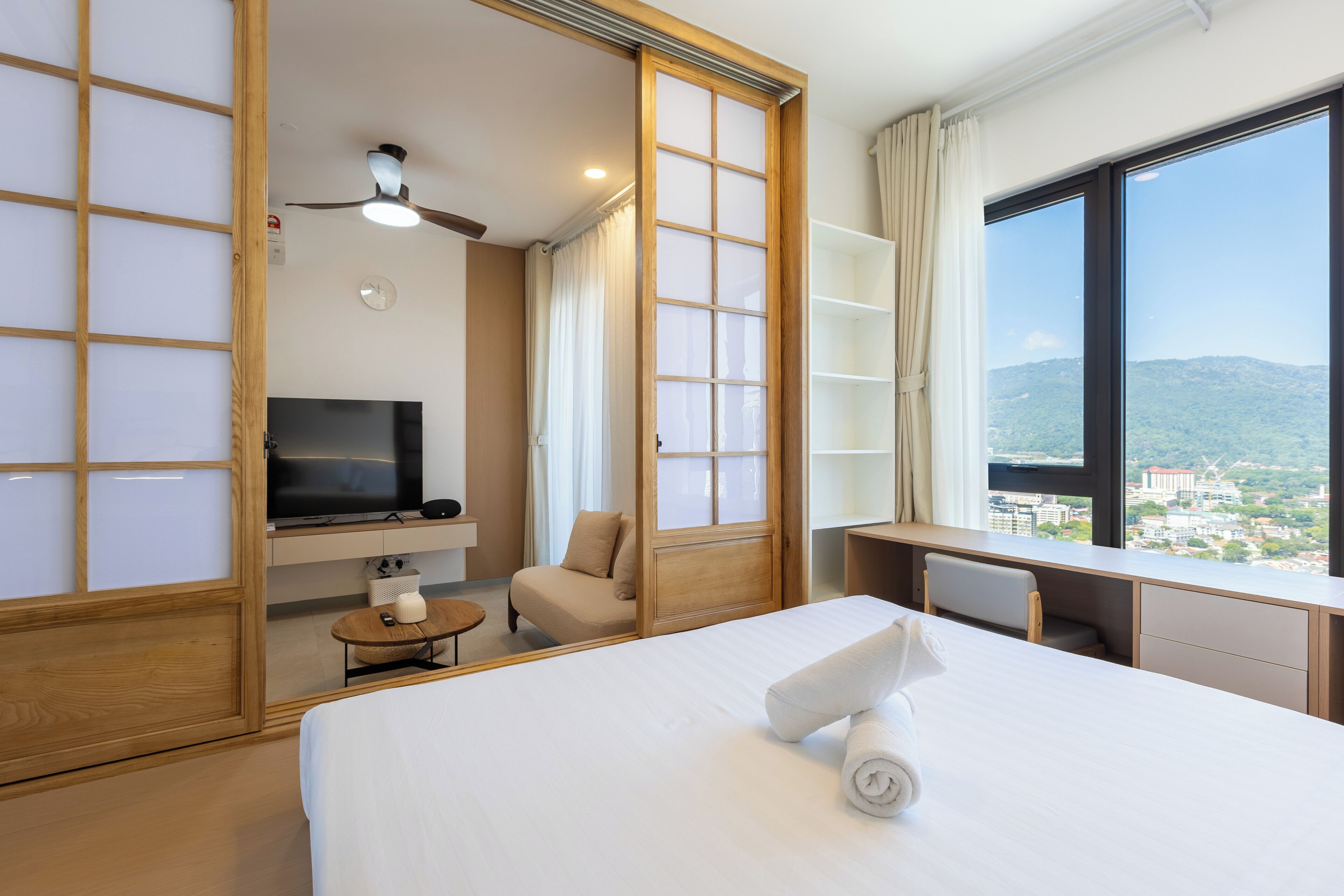 Quarto de hotel com cama, escrivaninha, televisão, cadeira e vista para a cidade.