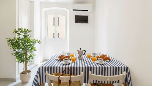 Uma área de refeições com uma mesa posta para o café da manhã, incluindo croissants e suco de laranja, e uma planta em vaso.