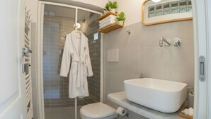 Uma casa de banho moderna com cabine de duche, sanita, lavatório e um roupeiro com roupão.