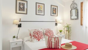 Quarto de hotel bem arrumado, com cama, duas mesas de cabeceira, manta vermelha e luminárias fixadas na parede.