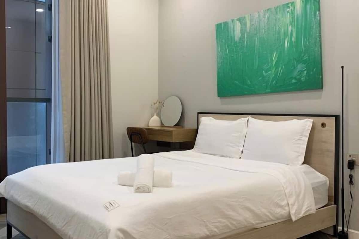 Quarto de hotel com cama, espelho, pintura abstrata verde e janela com cortinas.