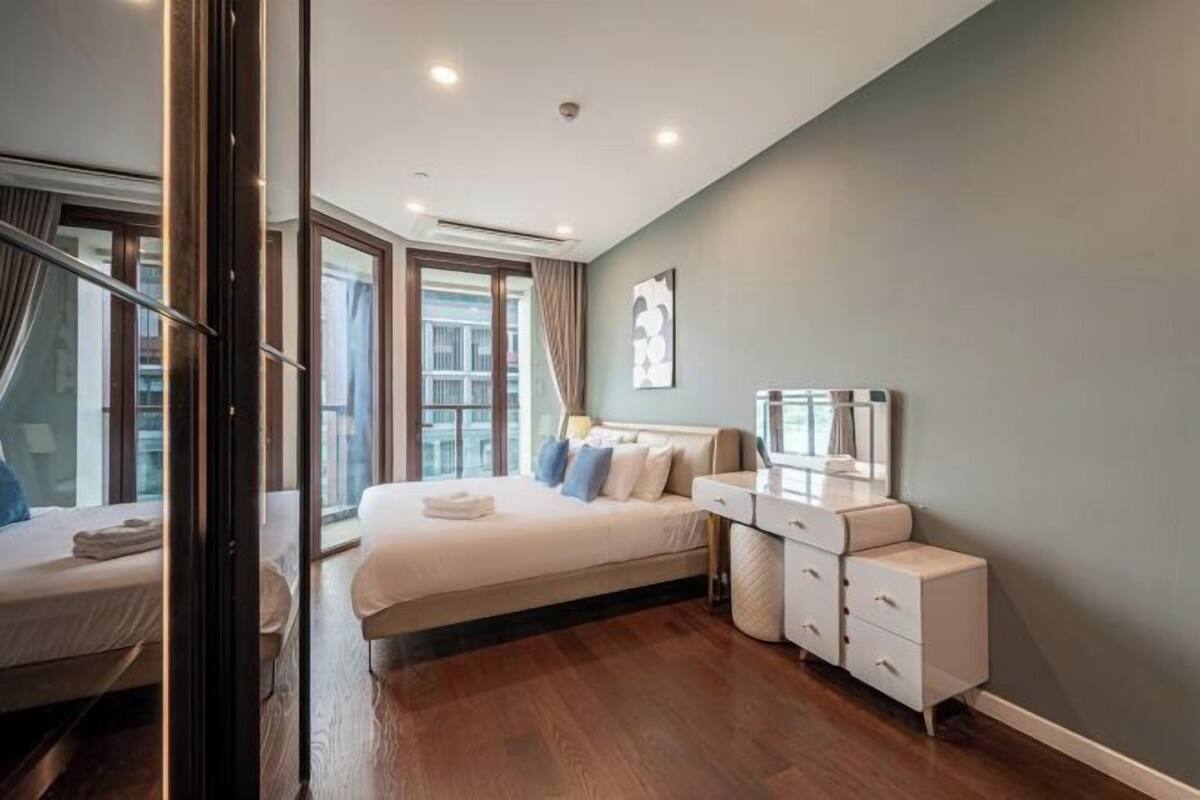 Quarto de hotel moderno com uma cama grande, mesa de cabeceira, cômoda e janela com cortinas.