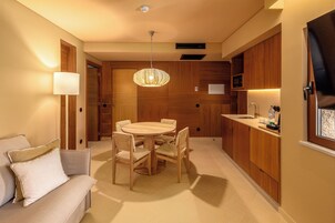 Quarto de hotel moderno com uma mesa de jantar redonda, armários de madeira, um sofá e um lustre.