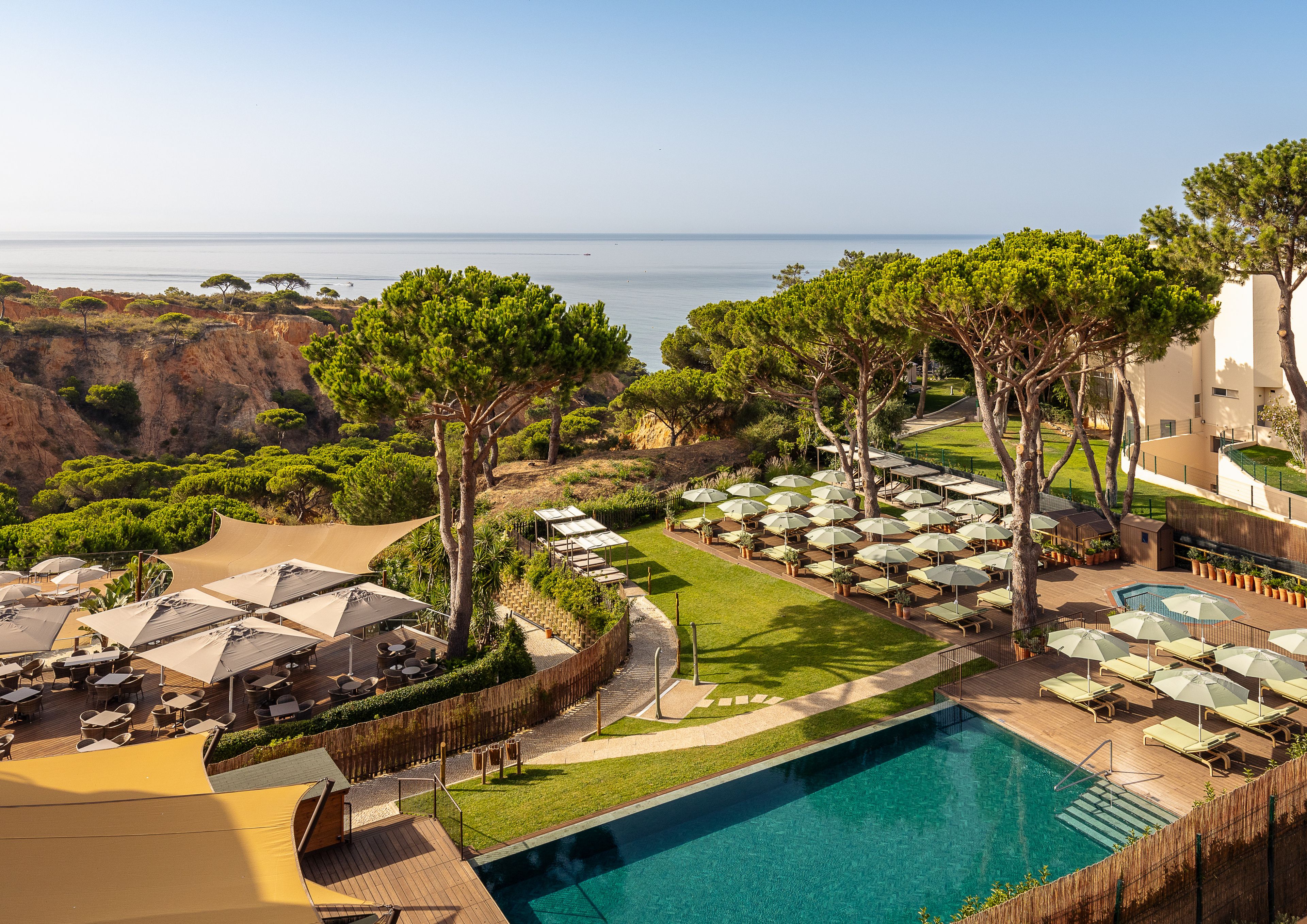 Área da piscina com guarda-sóis, espreguiçadeiras e vista para o oceano.