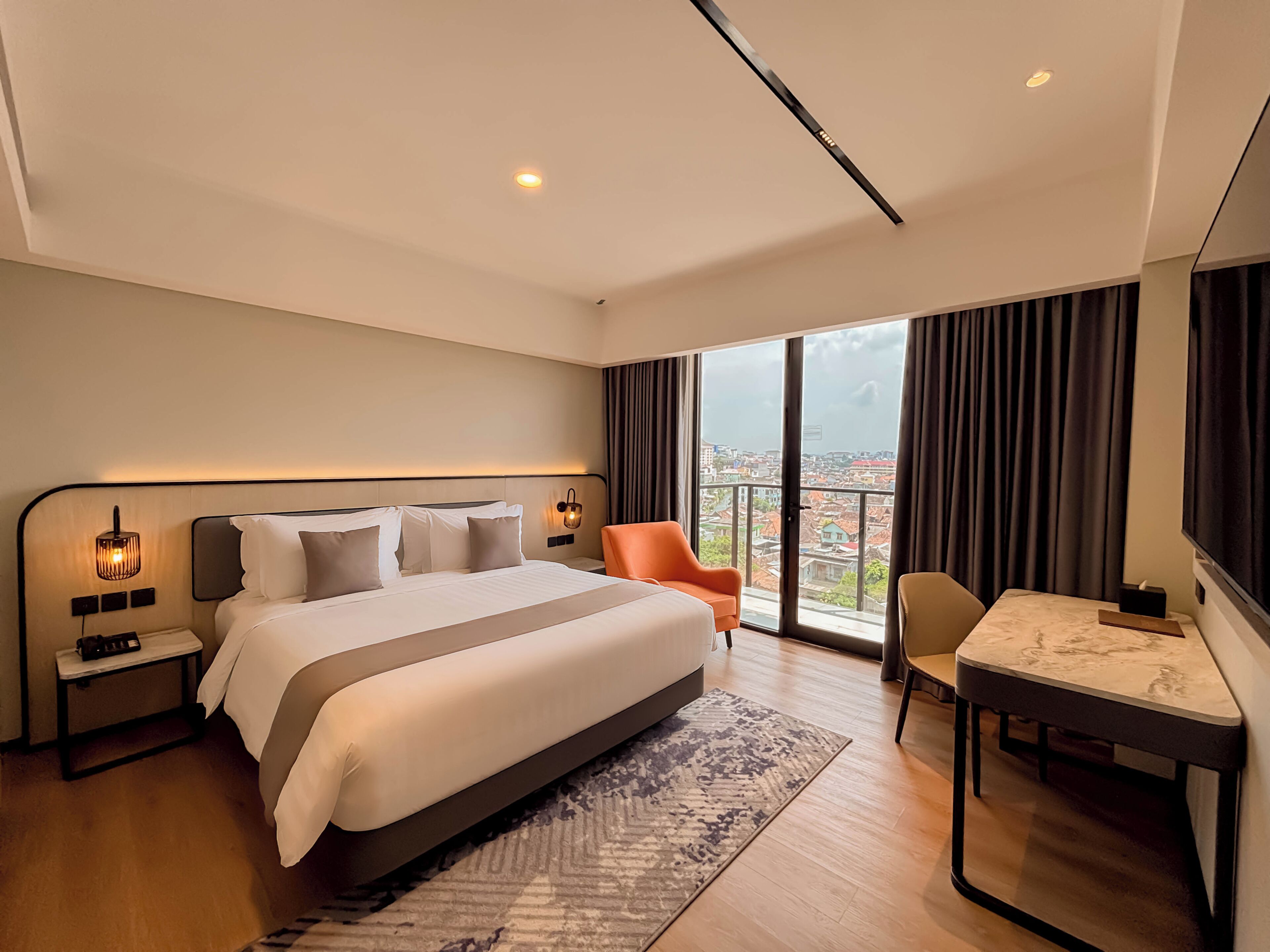 Quarto de hotel moderno com uma cama grande, uma escrivaninha, uma cadeira e vista para a cidade.
