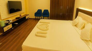 Quarto de hotel moderno com uma cama grande, televisão de tela plana na parede, guarda-roupa e duas poltronas.