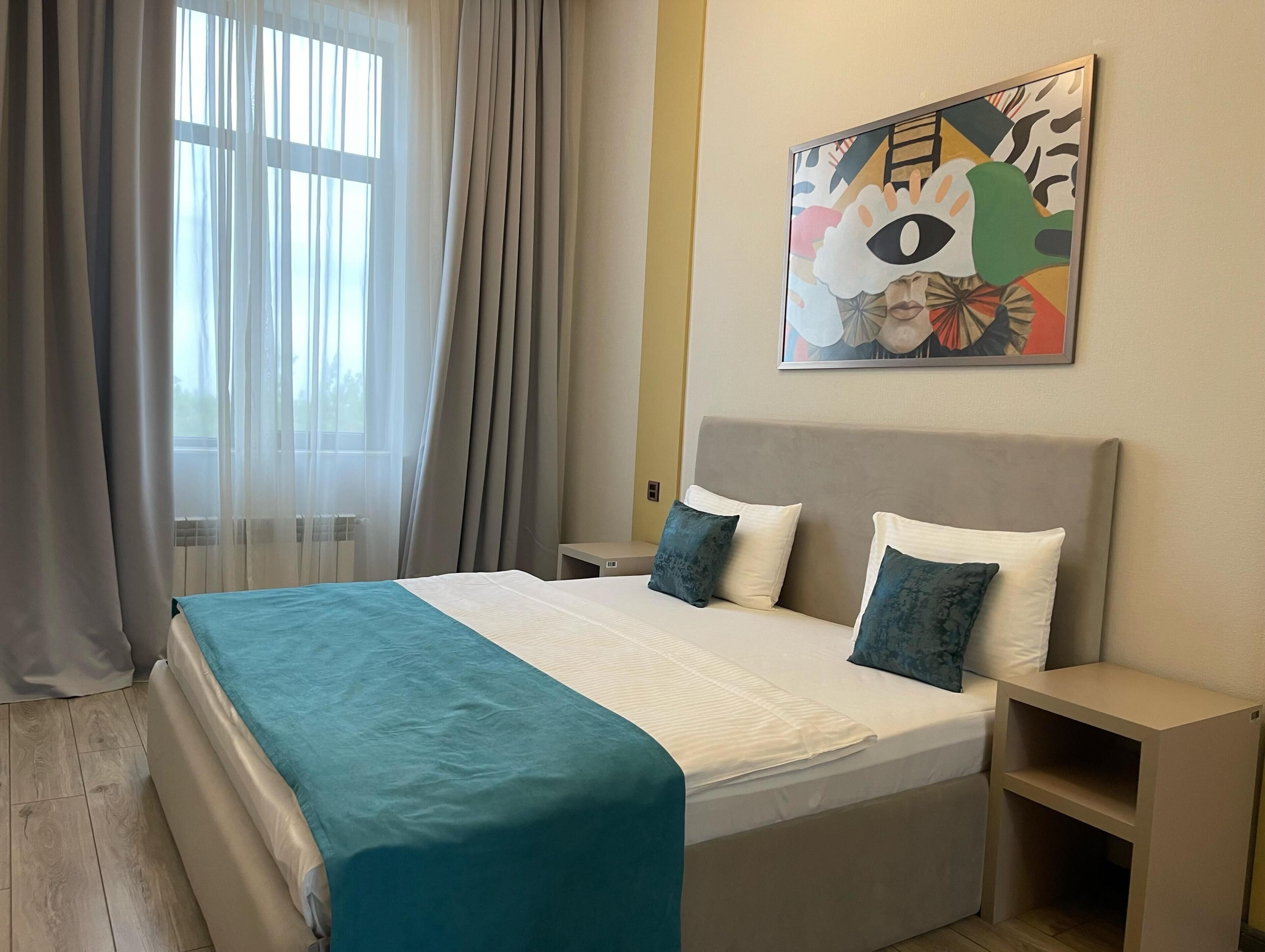 Quarto bem arrumado com cama, duas almofadas, mesa de cabeceira e janela com cortinas.