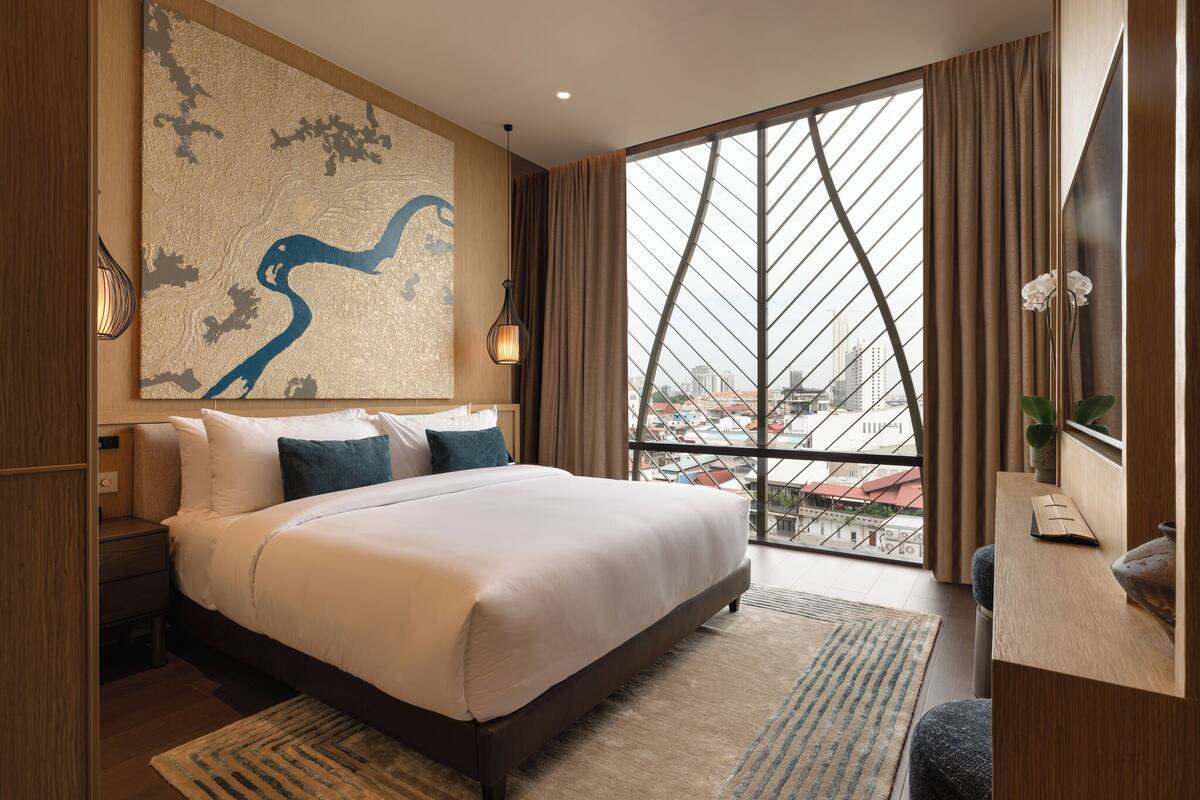 Quarto de hotel com uma cama grande, vista da cidade e um objeto decorativo na parede.