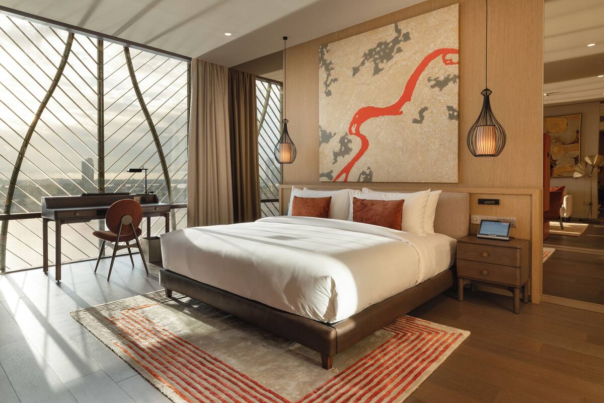 Quarto de hotel moderno com uma cama grande, uma escrivaninha e um laptop sobre a mesa de cabeceira.