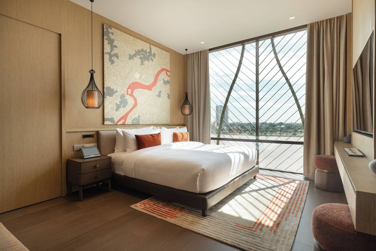 Quarto de hotel moderno com uma cama grande, uma escrivaninha, um computador portátil e vista para a cidade através de amplas janelas.