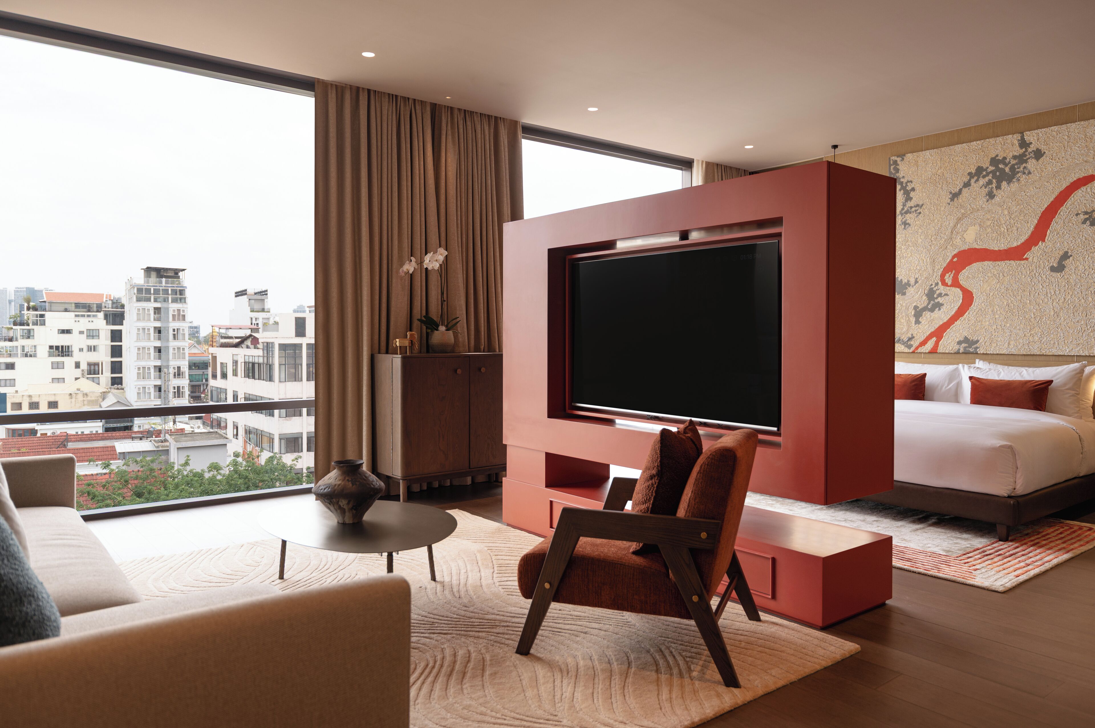 Quarto de hotel moderno com uma televisão grande, um sofá, uma poltrona e uma cama.
