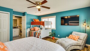Quarto com beliche, escrivaninha, cadeira e ventoinha no teto.