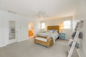 Um quarto com cama, um banquinho de vime, um ventilador de teto e uma escada de madeira encostada à parede.