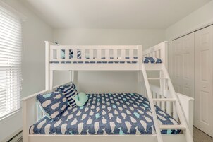 Uma cama beliche com colchão e almofadas estampadas, uma escada e uma janela com persianas.