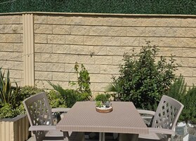 Pátio externo com mesa e cadeiras, cercado por um muro de pedra e diversas plantas.