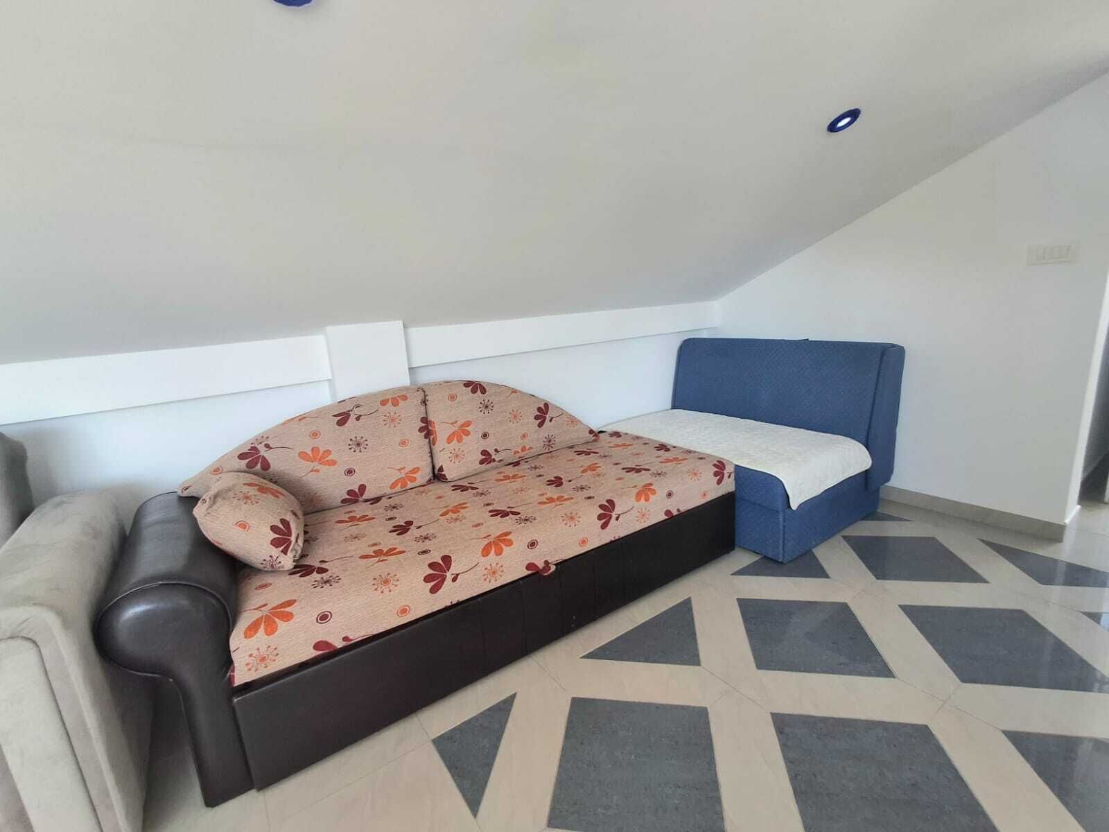 Quarto pequeno e moderno com um sofá-cama, uma cadeira azul e um tapete estampado.