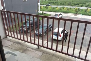 Varanda com grade de metal dando para um estacionamento com vários carros.